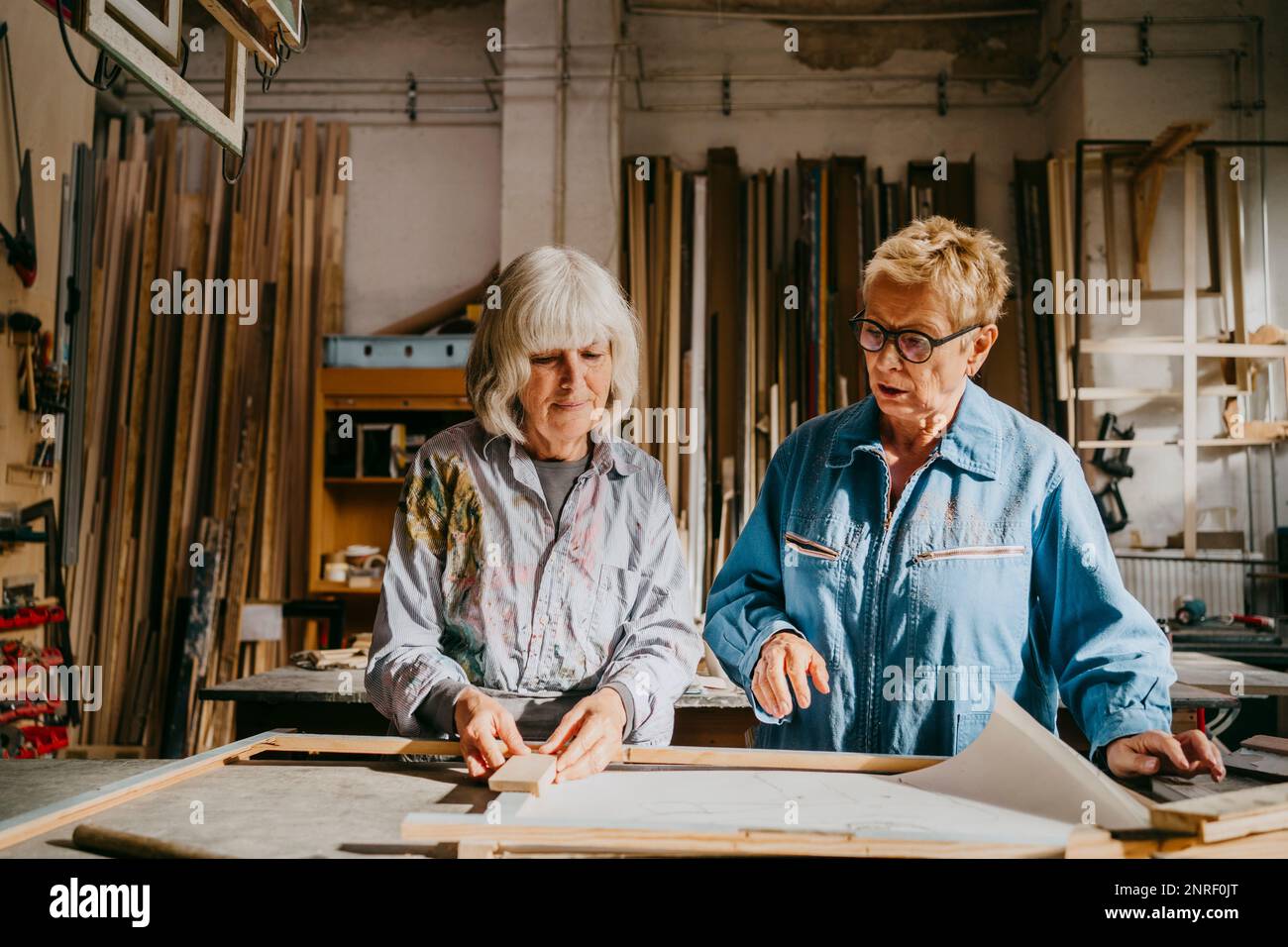 Senior female carpenters discussing with each other while working at ...