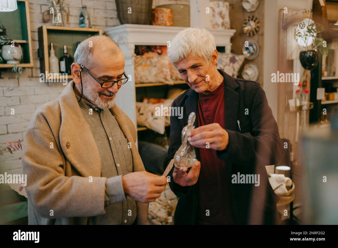 Senior male customer checking price tag of glass figurine held by owner ...