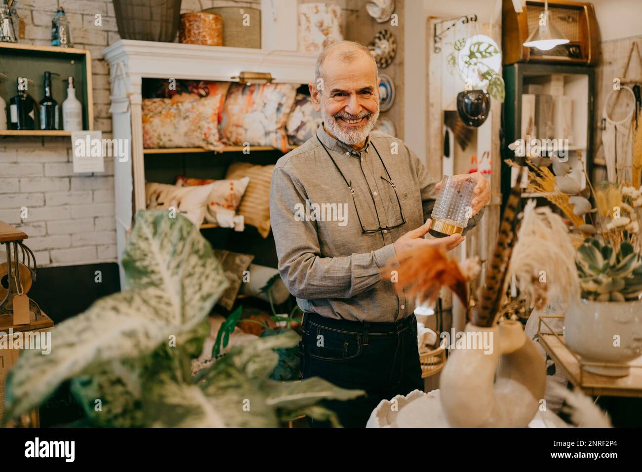Happy senior male owner showing glass decor at home interior store ...