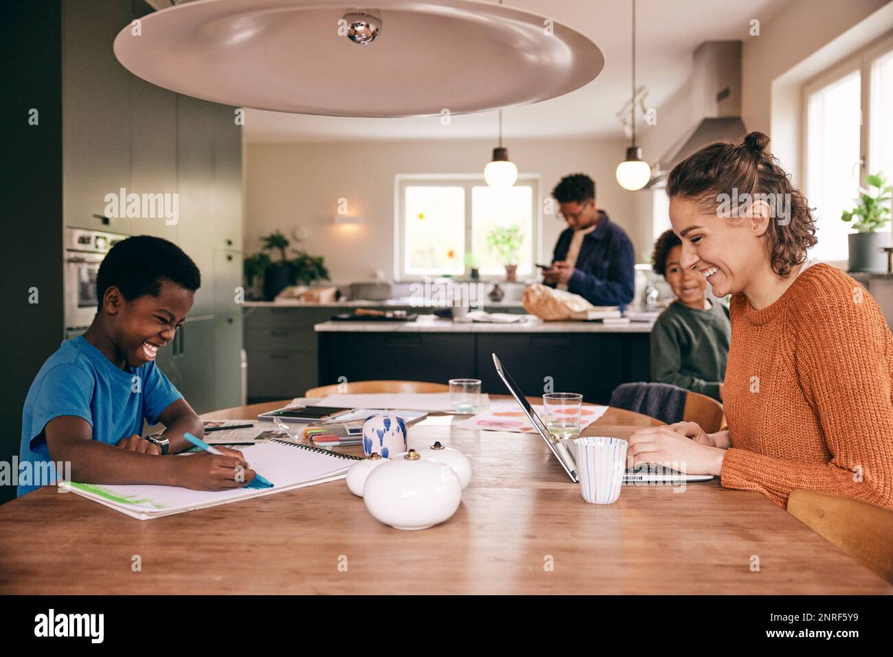 Happy mother using laptop with son coloring in book while sitting at ...