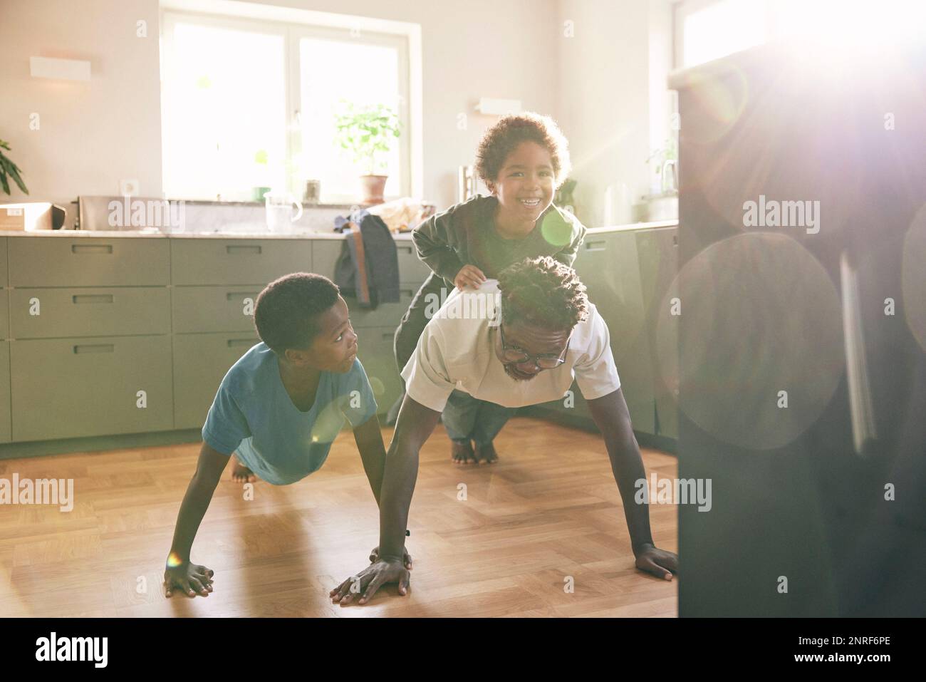 Father doing push-ups while carrying son on back in kitchen at home ...