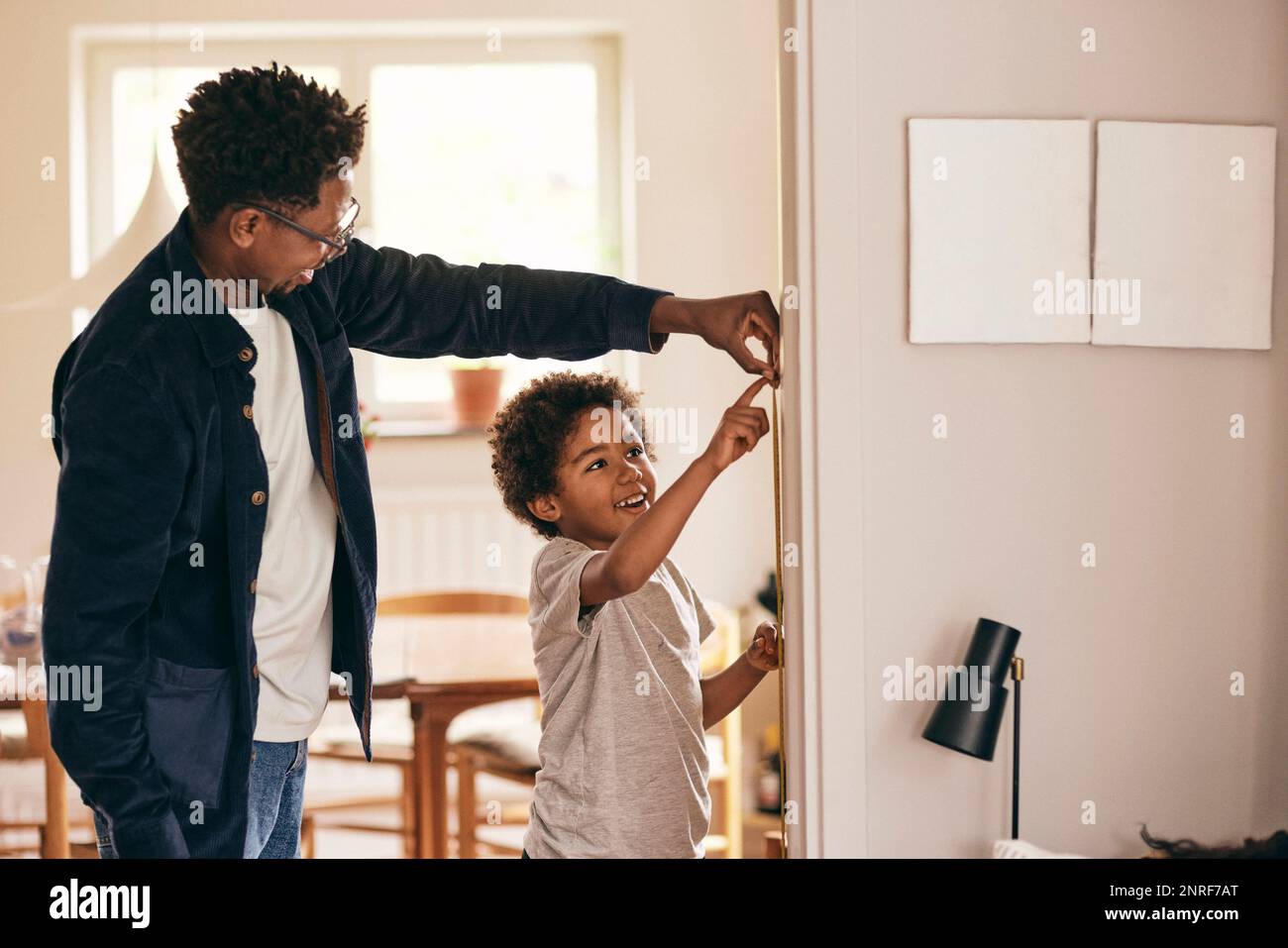 Happy father and son checking height while standing near wall at home ...