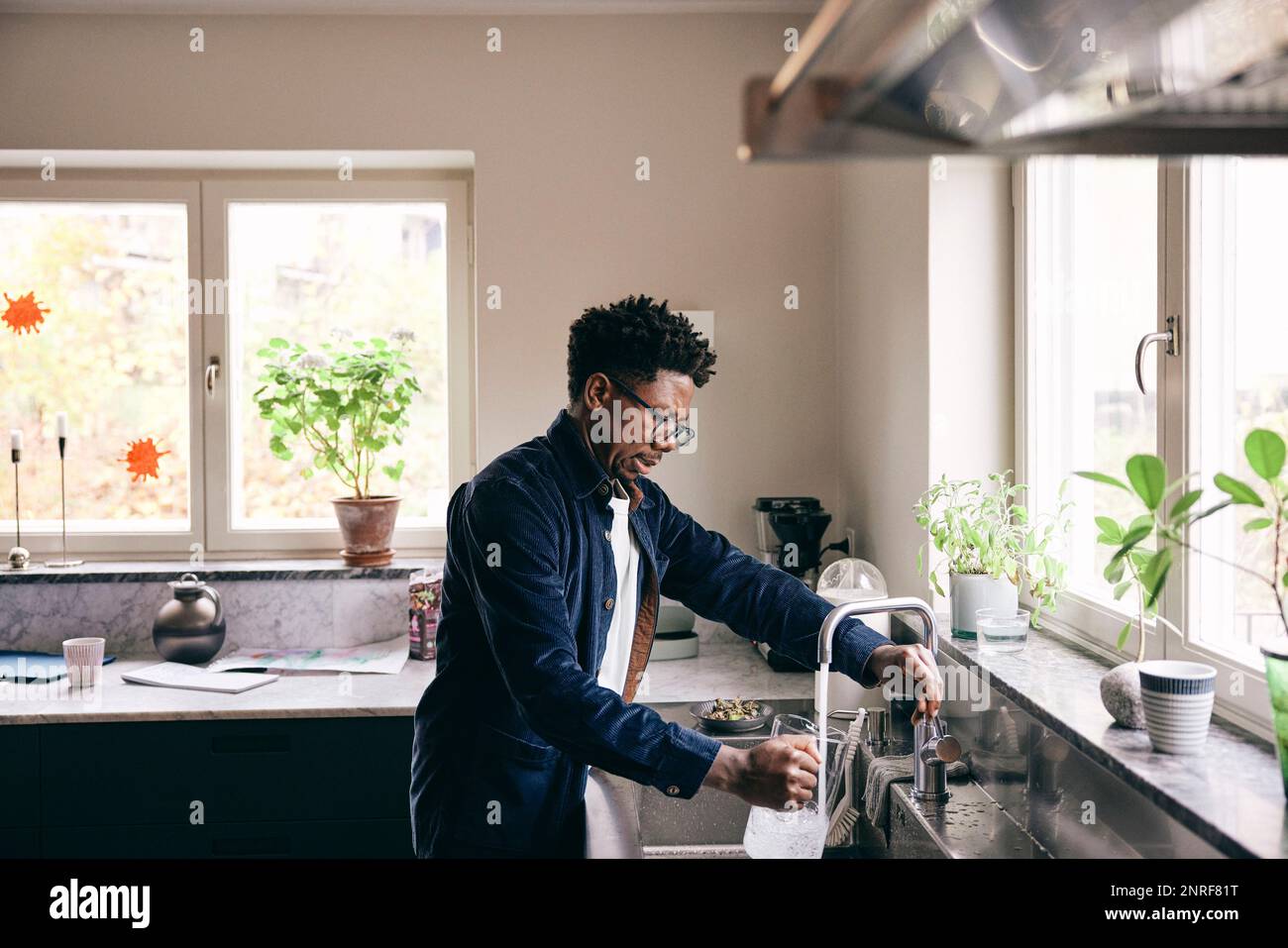 Side view of mature man filling pitcher from faucet in kitchen at home ...