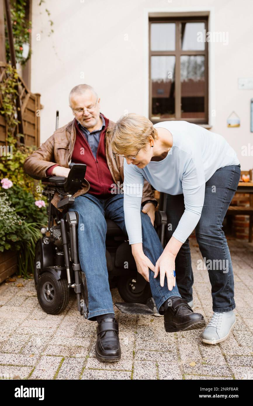 Full length of senior woman helping man with disability sitting in ...
