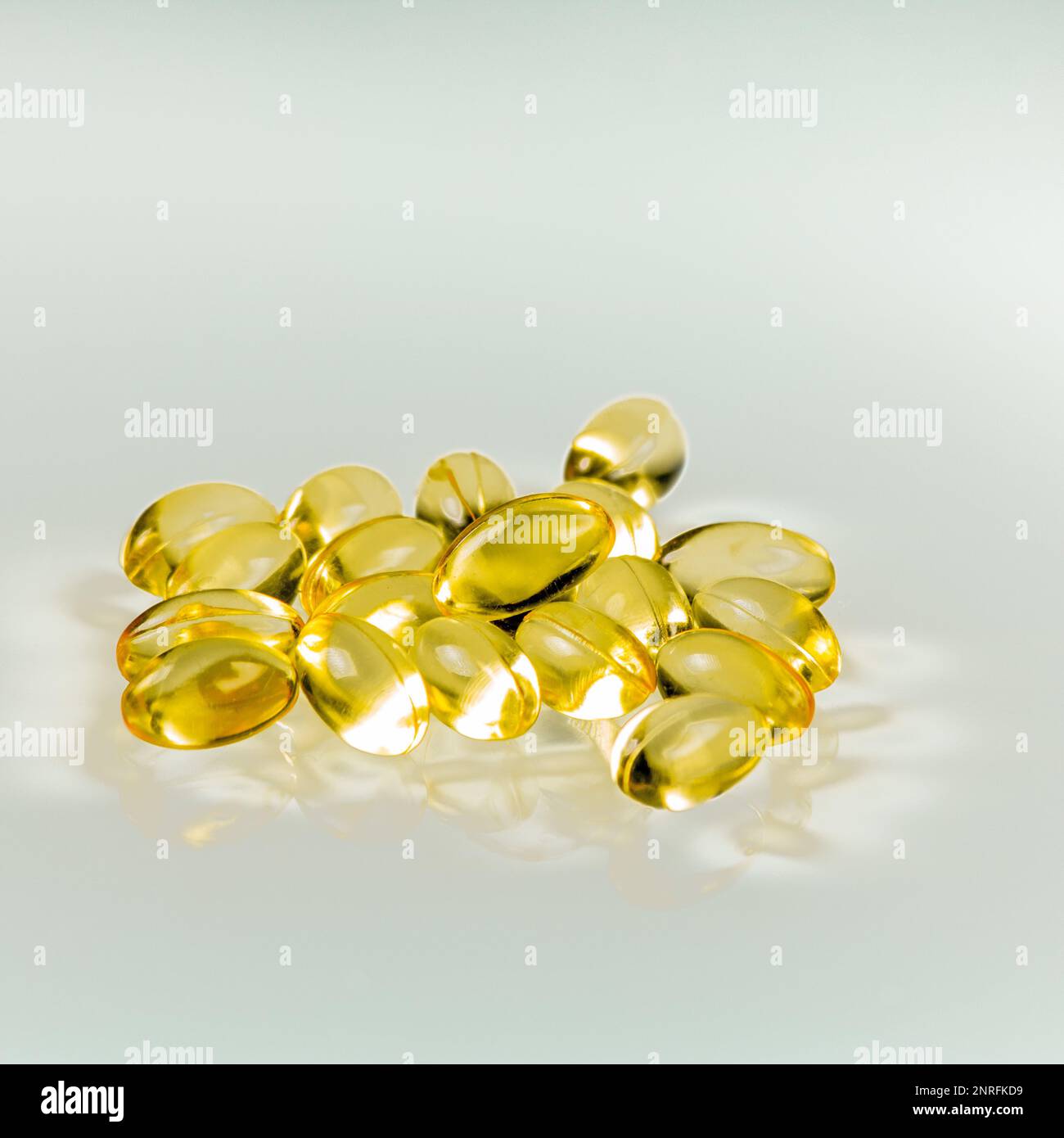 Pile of yellow fish oil gel capsules reflected on glass background ...