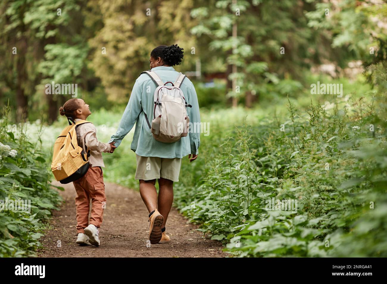 Back view of joyful mother and daughter walking on nature trail together holding hands, copy ...