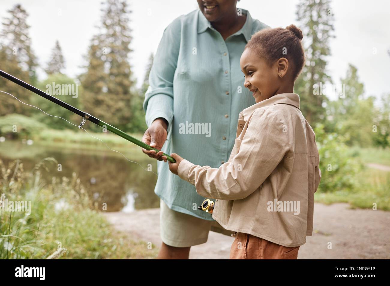 Side view portrait of happy little girl fishing with parent by river in ...