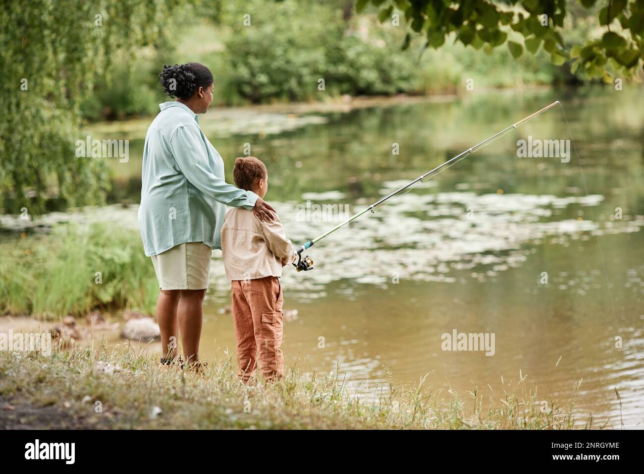 Back view of mother and daughter fishing together by lake in beautiful ...