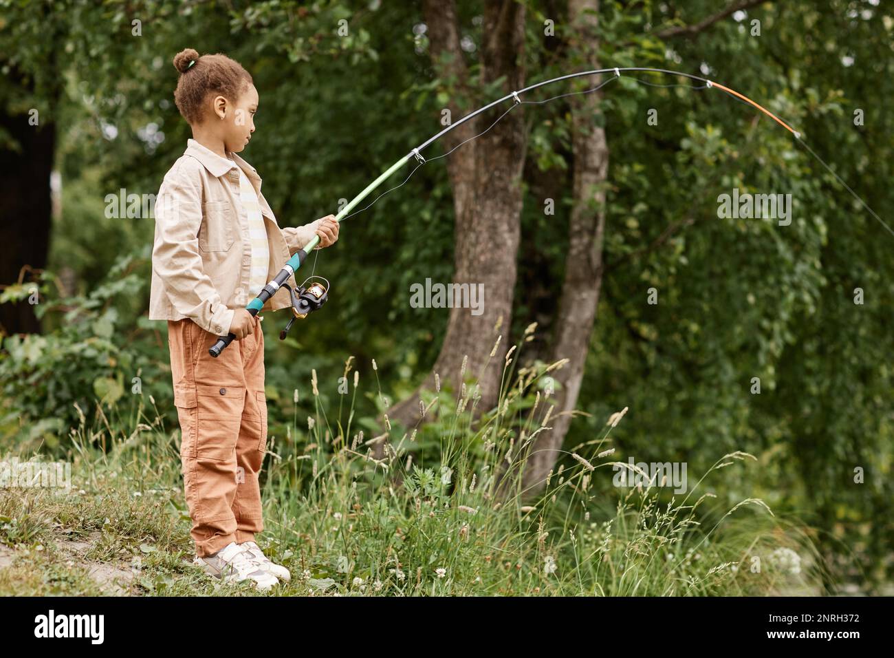 Full length side view portrait of black little girl fishing by river in ...