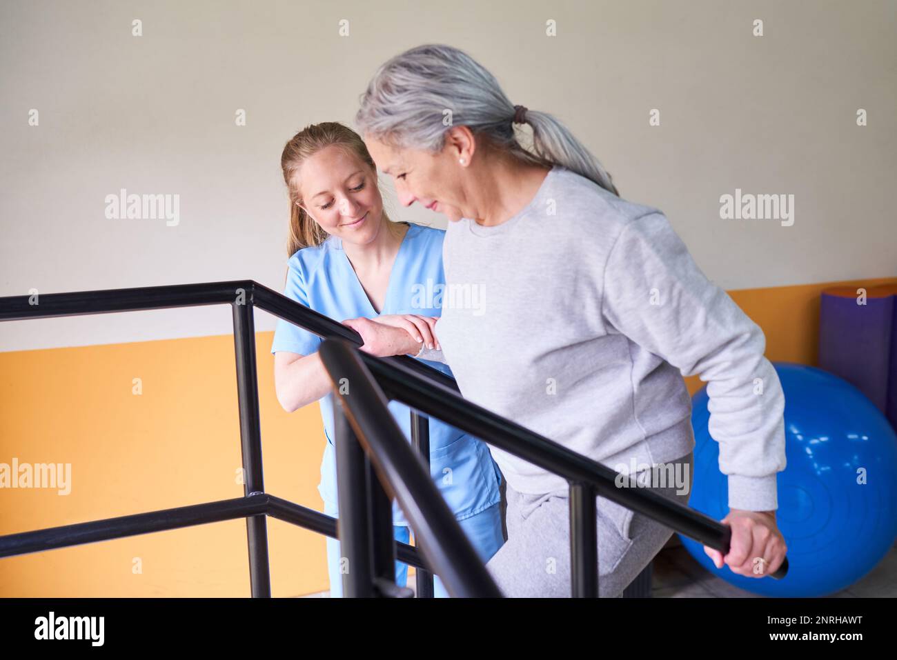 Smiling Female Caregiver Assisting Senior Woman In Movement Therapy At