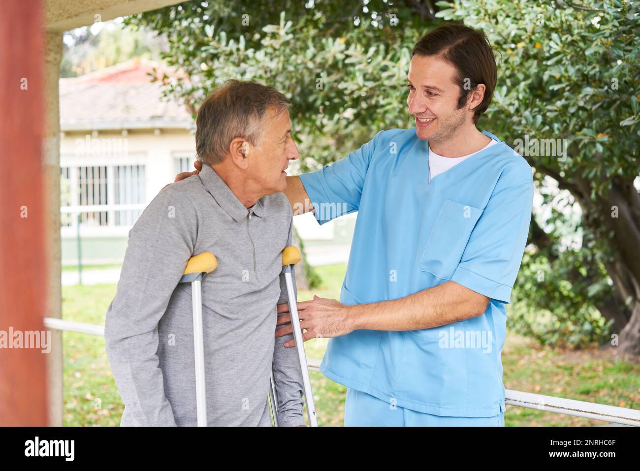 Smiling male nurse supporting disabled senior man to walk in garden ...