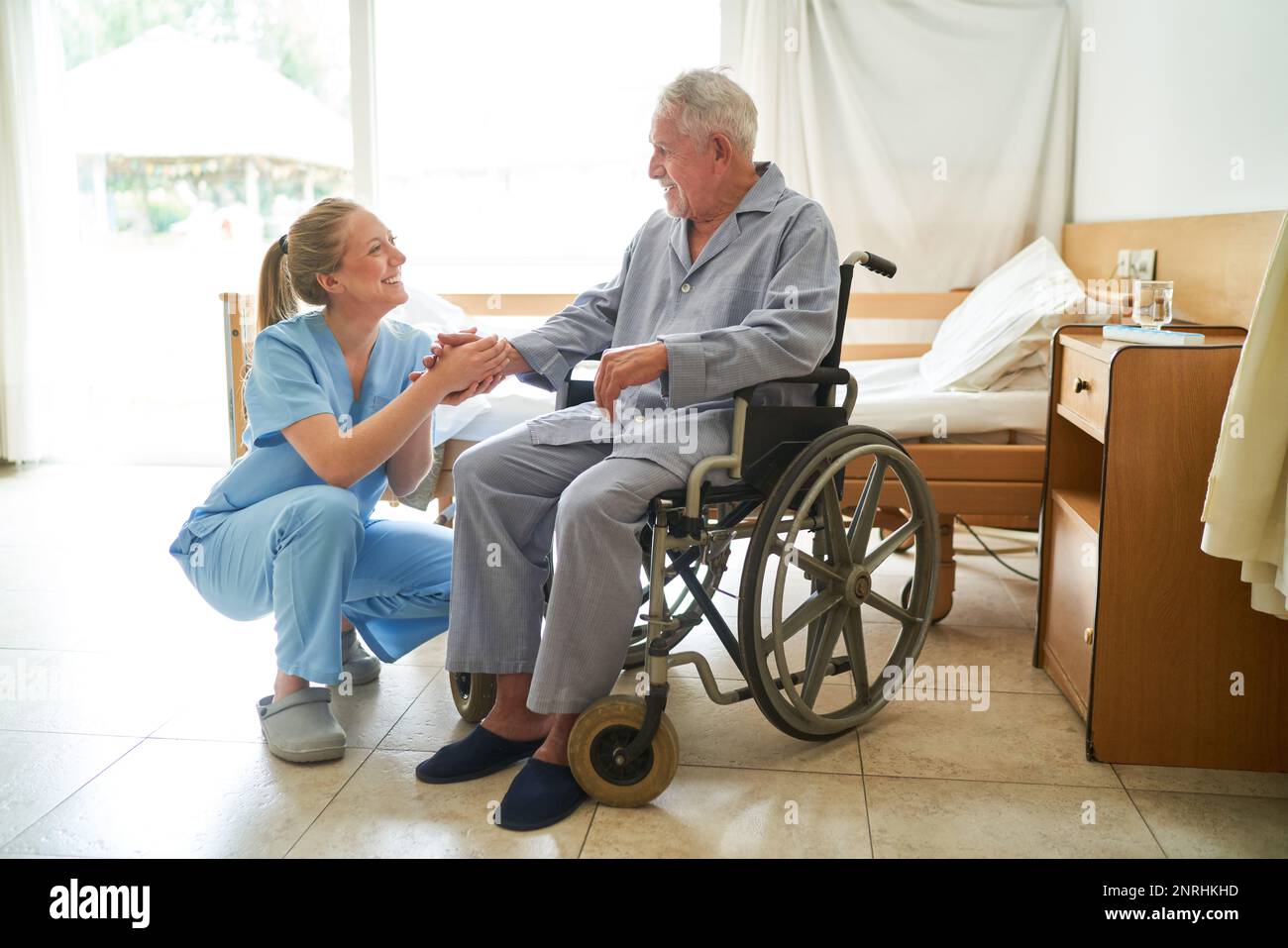 Smiling caring nurse holding hand of senior man sitting in wheelchair ...