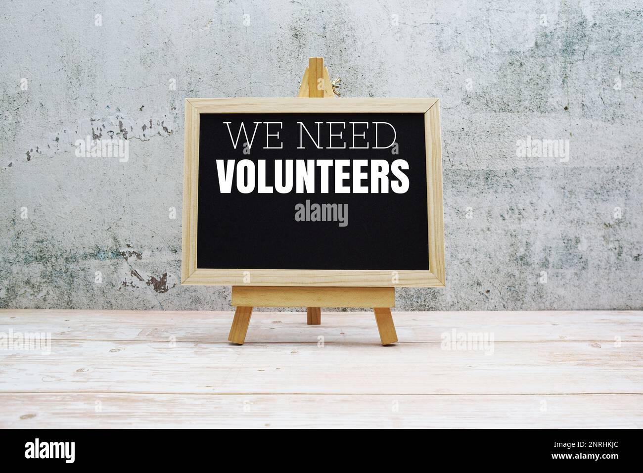 We need Volunteers text on the blackboard set on wooden floor and brick ...