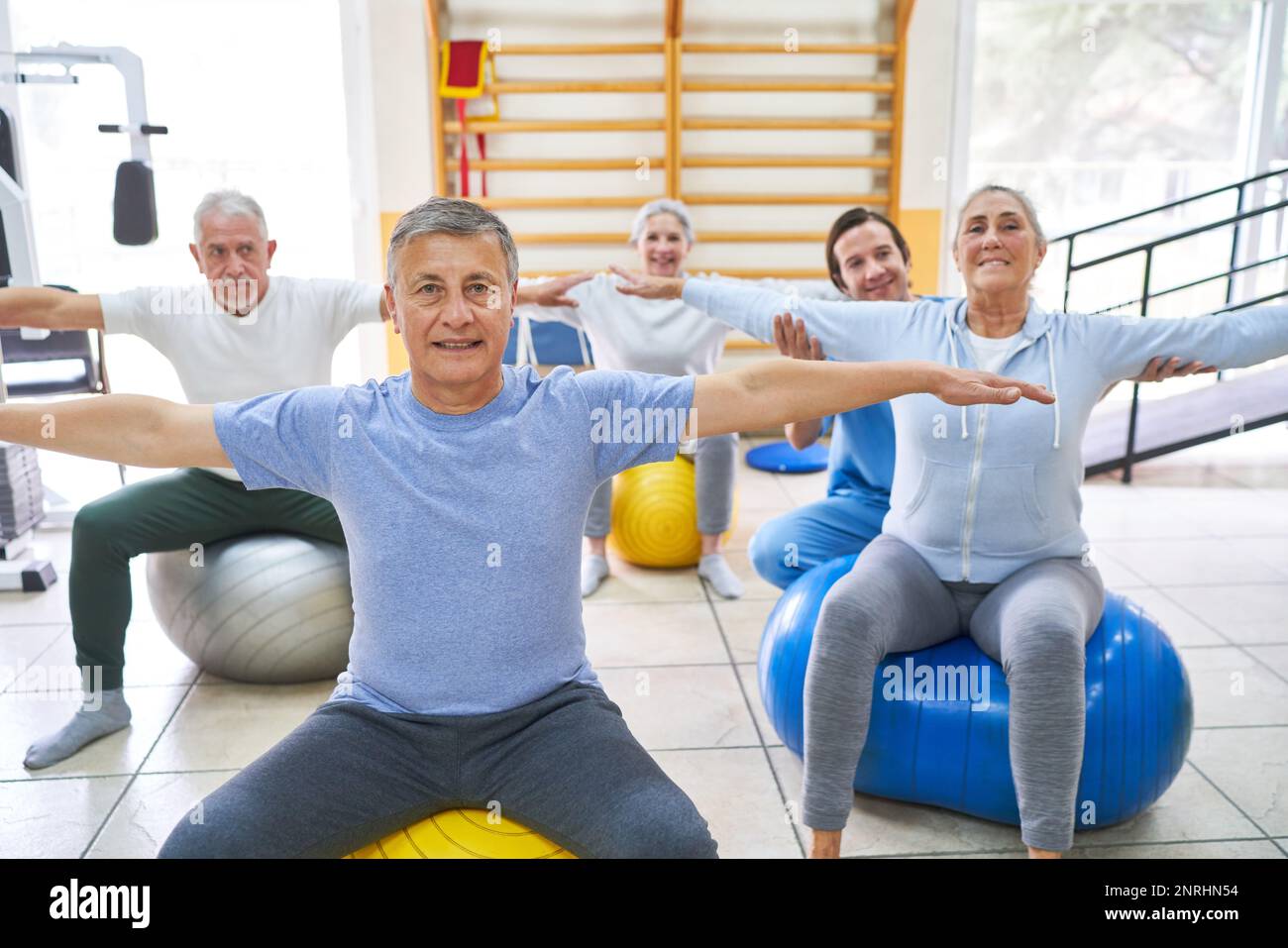 Group of elderly people exercising on fitness ball while therapist ...