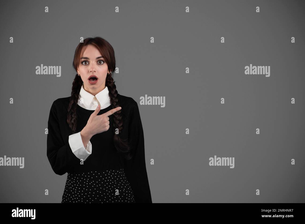 Shocked young female student in gothic black clothes with pigtails with open mouth point finger ...