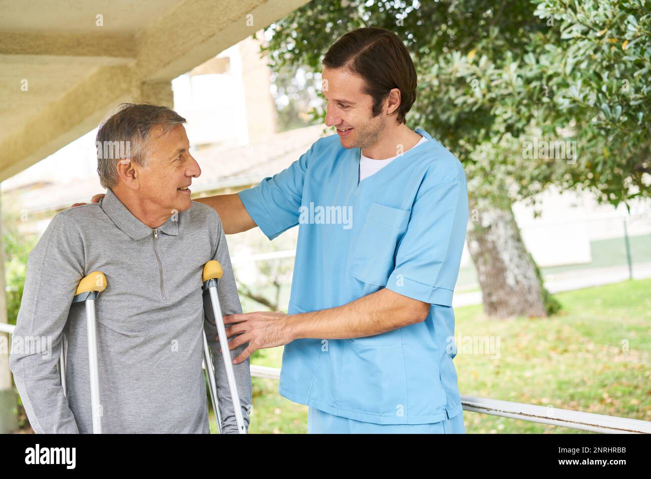 Smiling male nurse supporting elderly man with disability while walking in garden Stock Photo ...