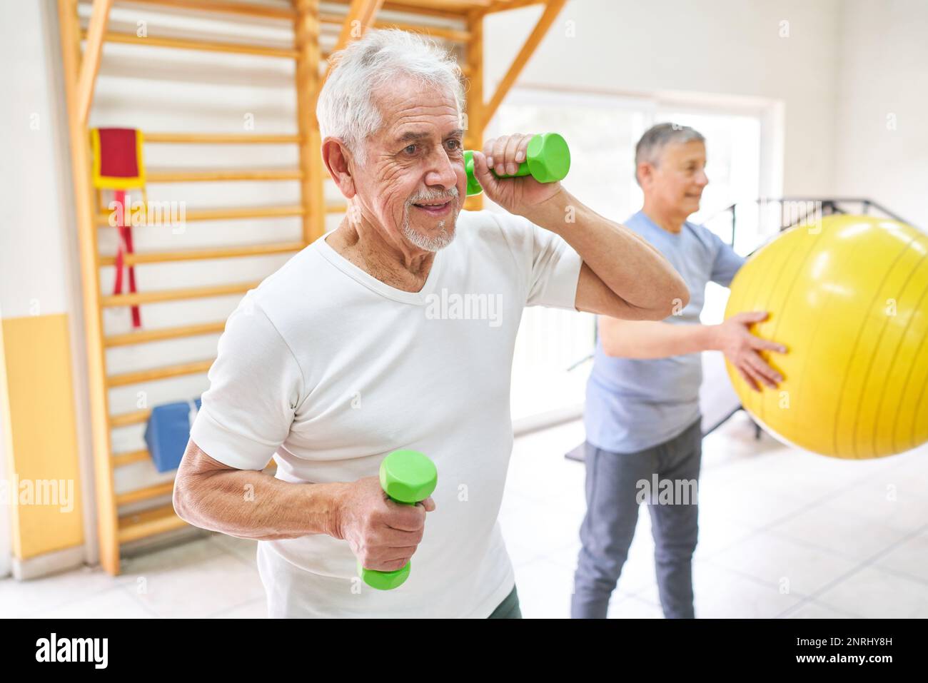 Senior man exercising with dumbbells during exercise class at ...