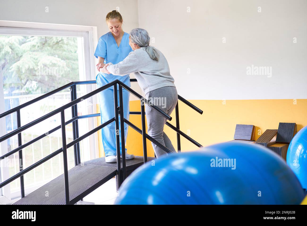 Female therapist assisting senior woman to climb inclined ramp at ...