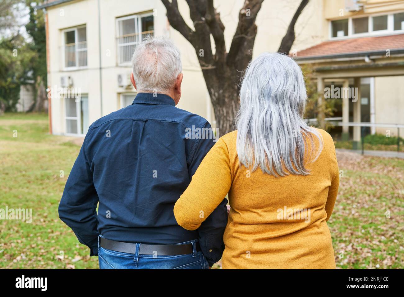 Rear view of elderly couple standing with hand in hand at garden of ...