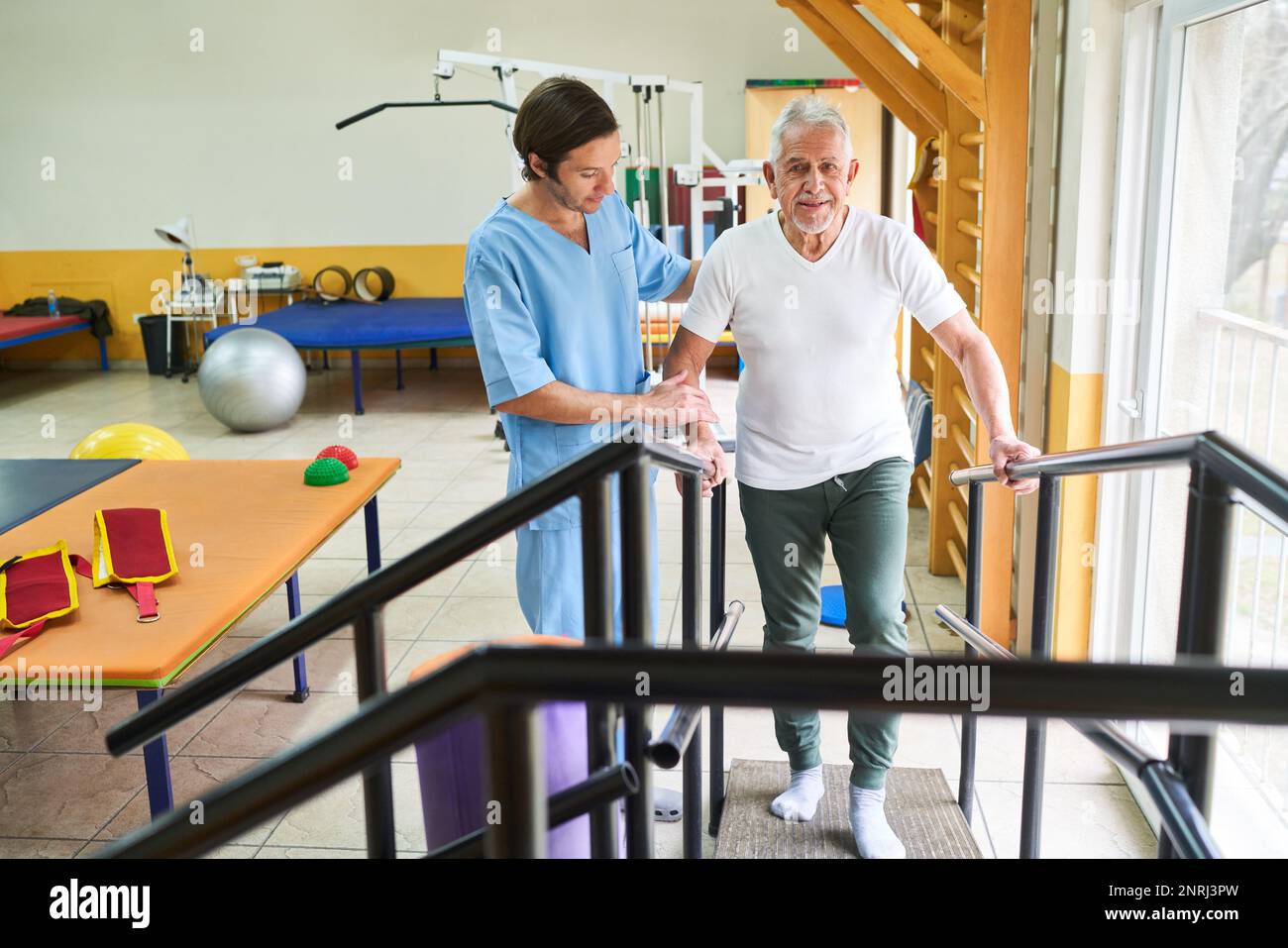 Male physiotherapist assisting elderly man in movement therapy at rehab ...