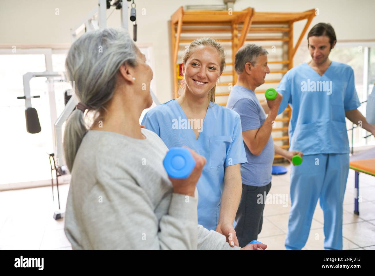 Smiling female nurse assisting elderly woman exercising with dumbbell ...