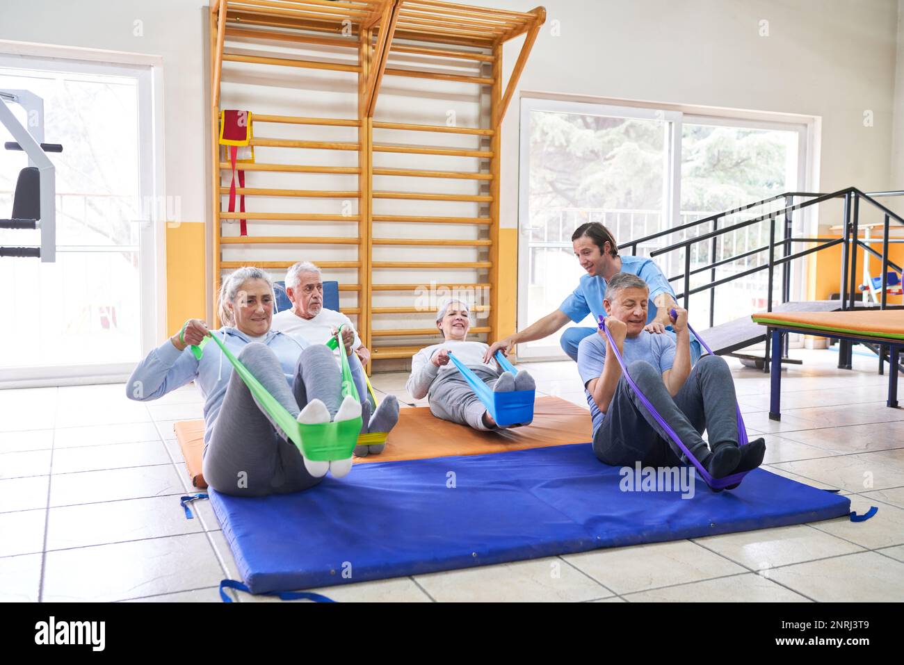 Male therapist assisting group of elderly people doing workout with ...