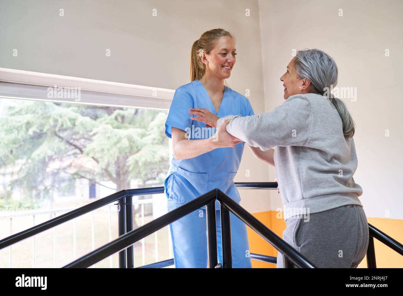 Smiling young female physiotherapist assisting elderly patient in ...