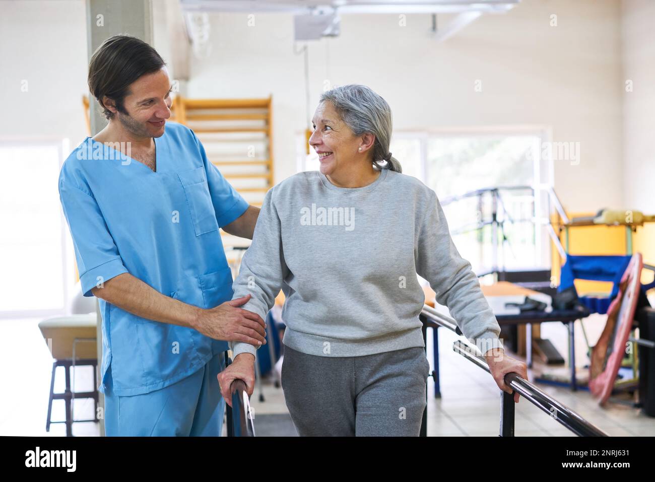 Male therapist assisting elderly woman in movement therapy at ...