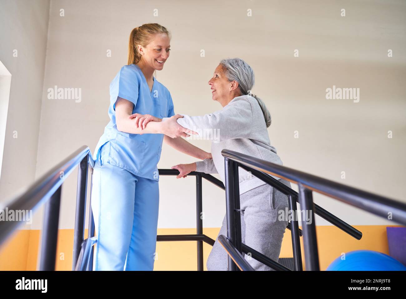 Smiling young female therapist assisting senior woman in movement ...