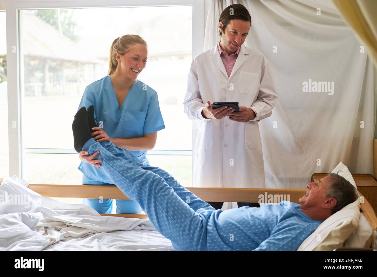 Doctor standing by smiling female nurse lifting legs of senior man ...