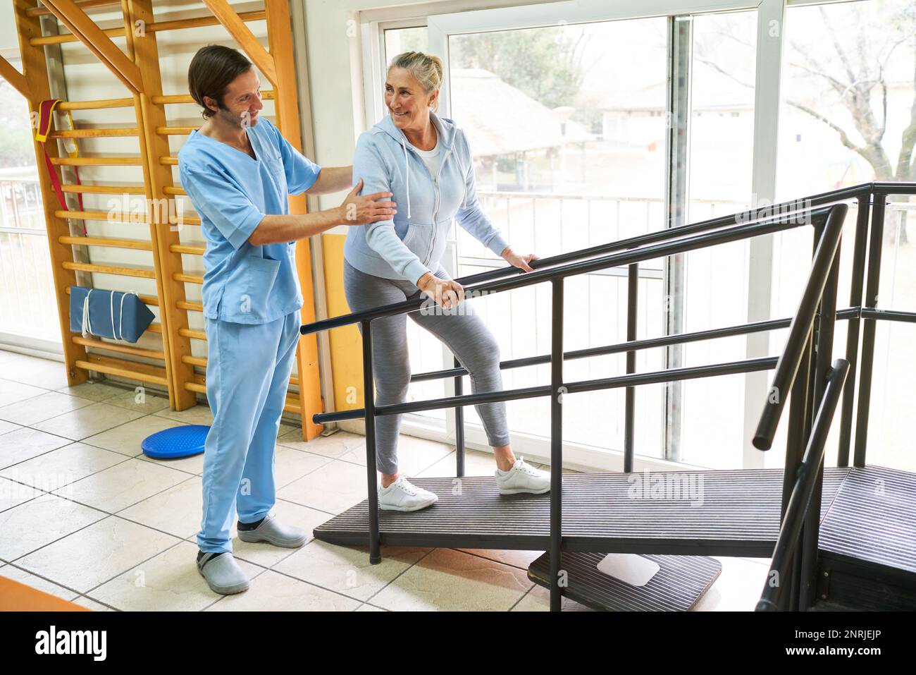 Male caregiver assisting smiling senior woman on ramp during movement ...
