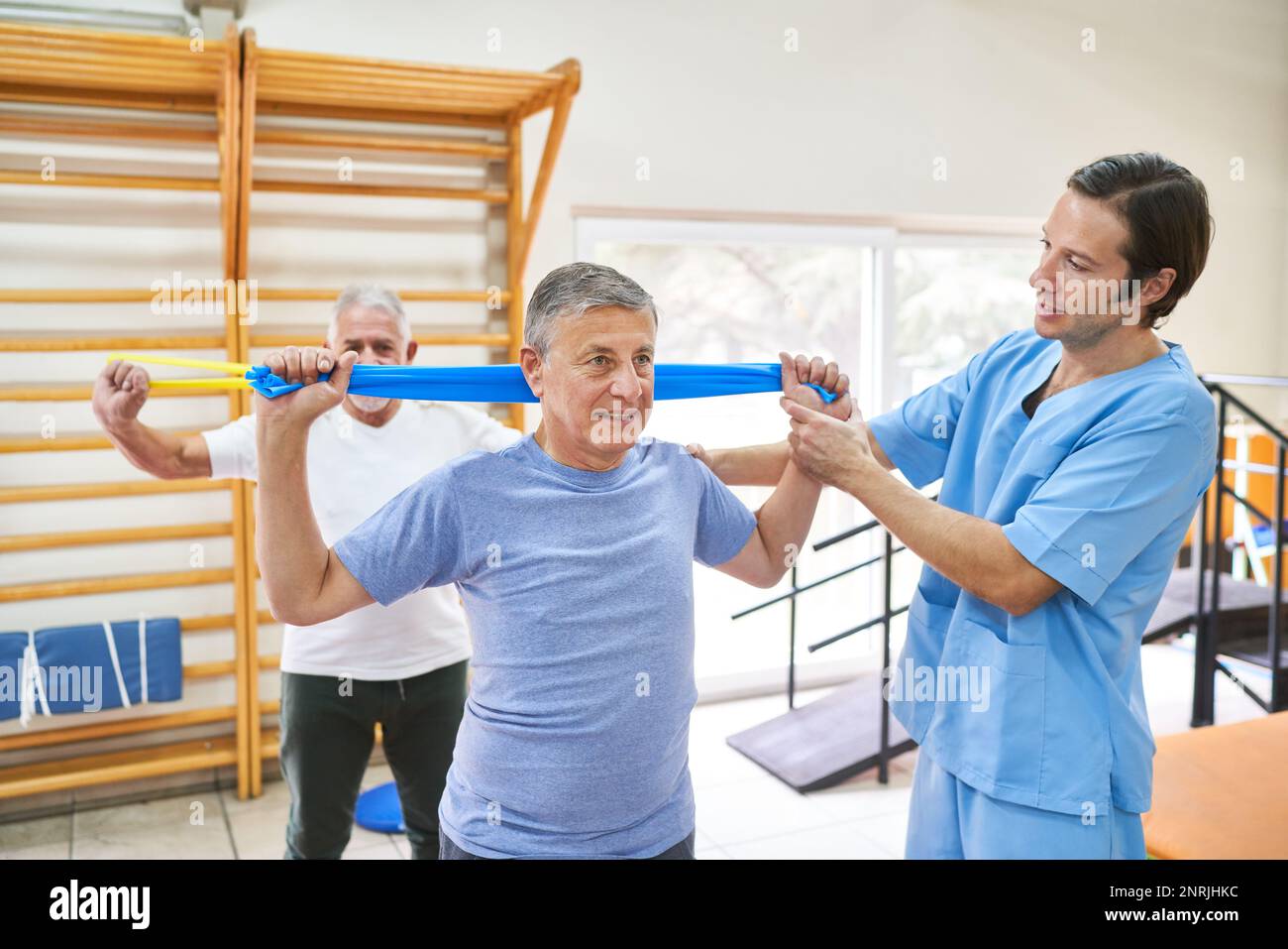Male therapist assisting elderly man in workout with resistance band at ...
