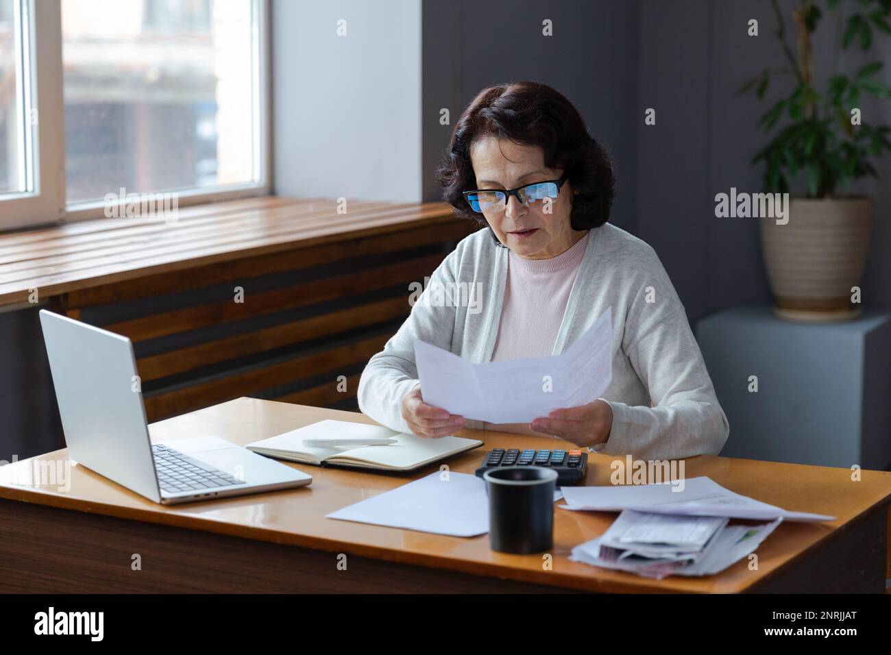 Middle aged senior woman sit with laptop and paper document. Pensive ...