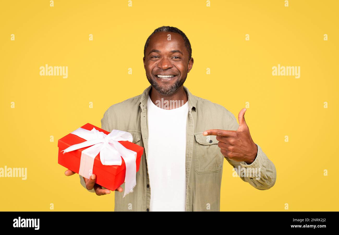 Happy middle aged black man pointing finger at gift box, recommends ad ...