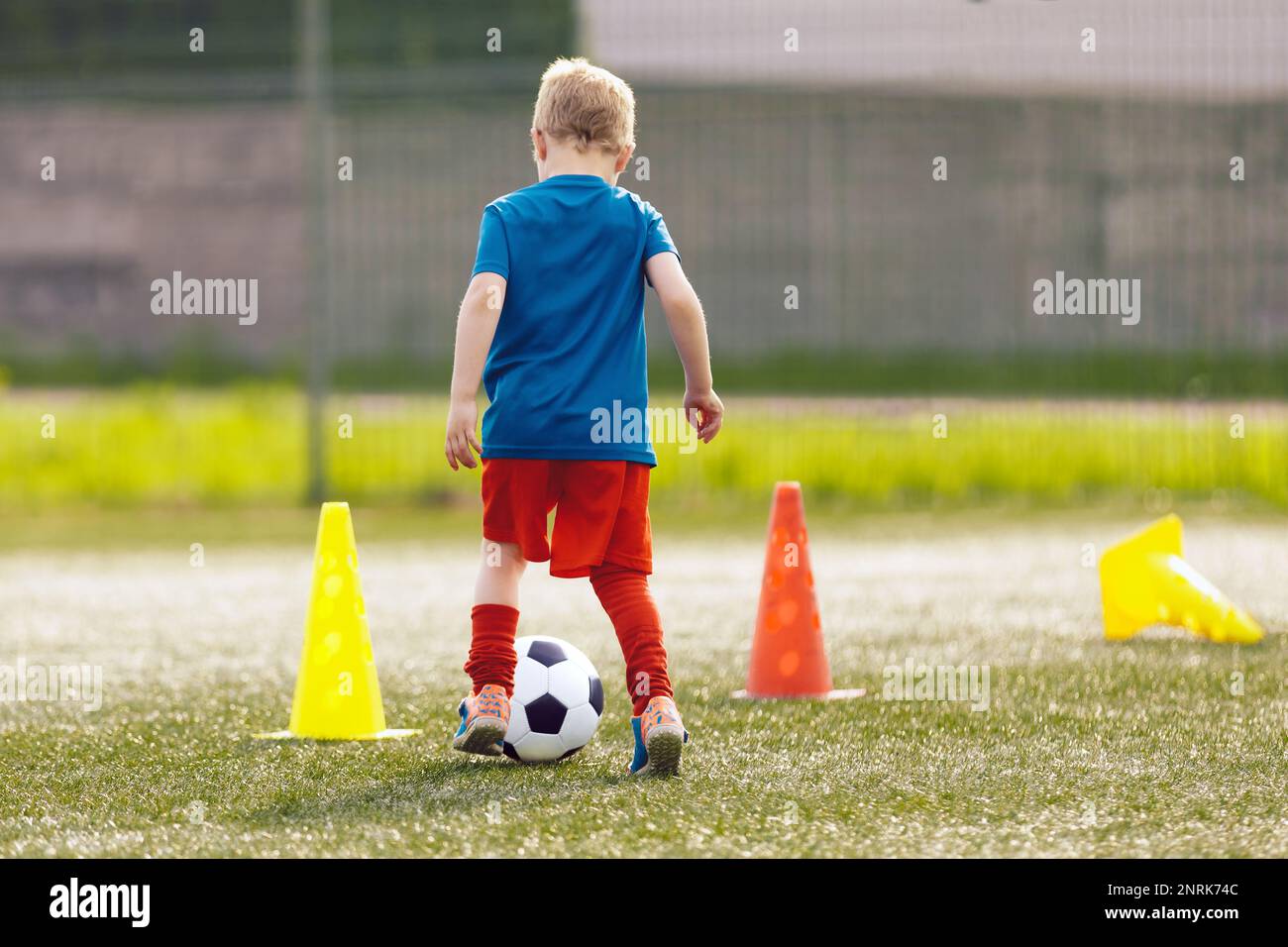 Lillte boy improving soccer skills by running the ball in slalom cones ...