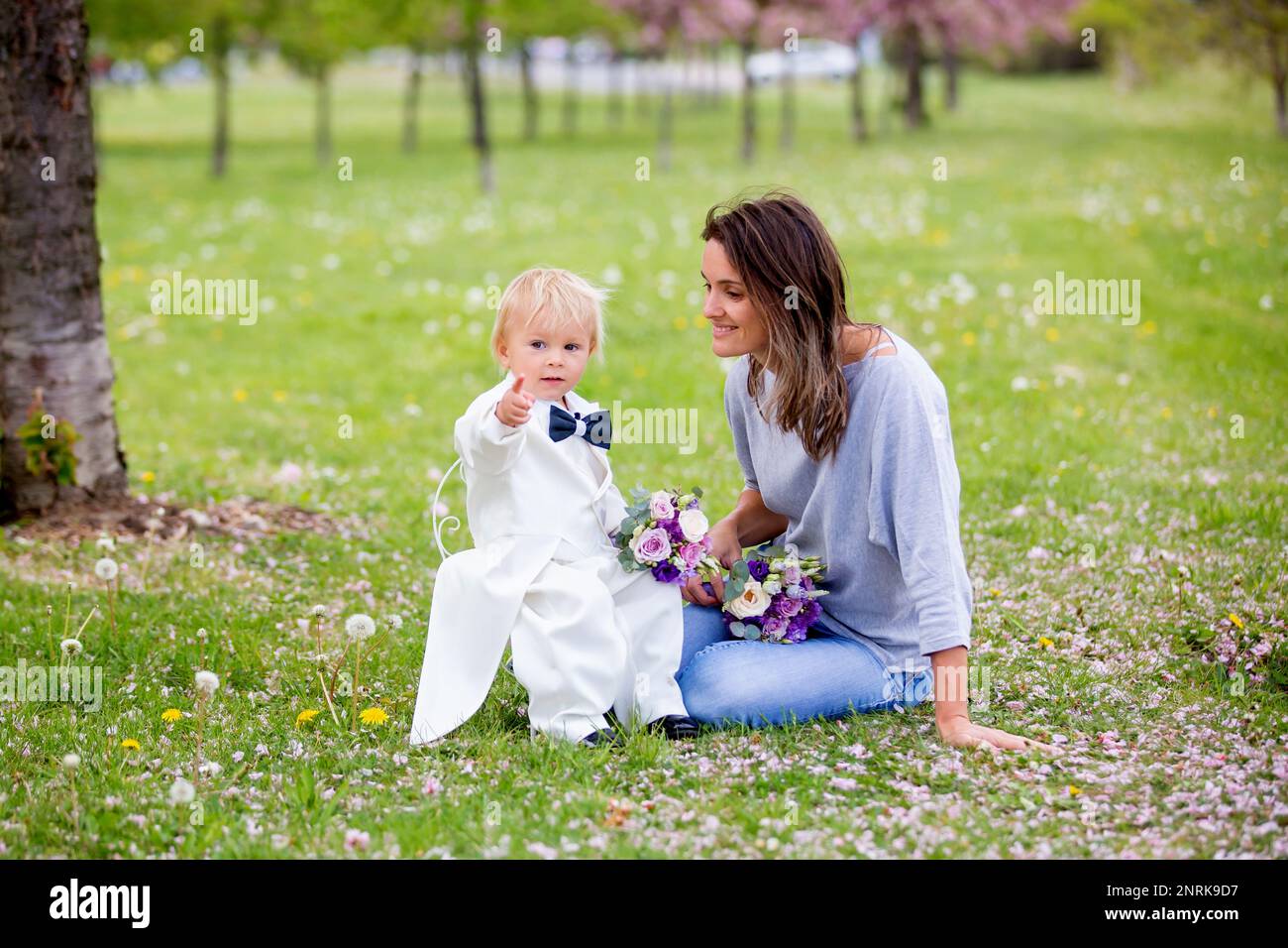 Beautiful toddler boy, dressed in white tuxedo, holding gorgeous flower ...