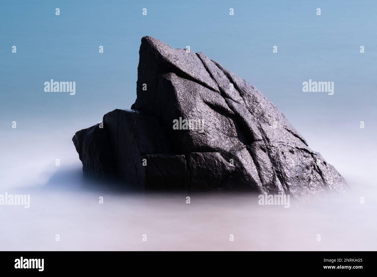 Isolated rock on a beach. Long esposure gives a silky smooth sea and ...