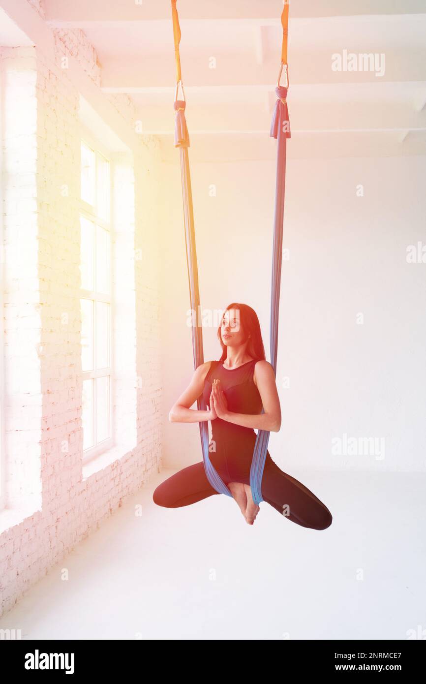 Fit young woman doing gravity fly yoga asana stretching exercises in ...