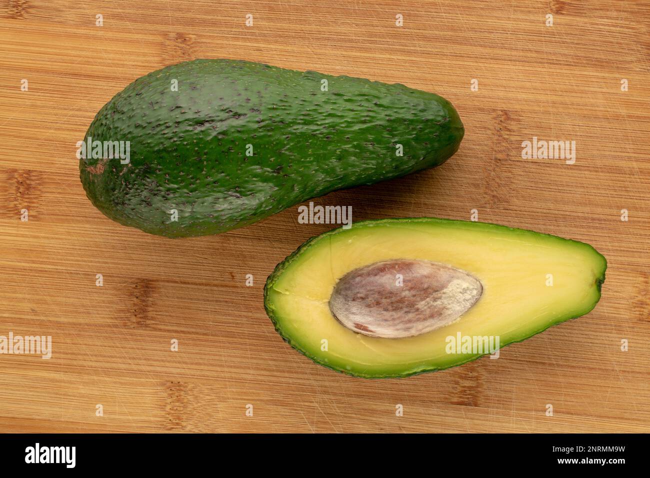 One whole and one half organic avocado on a bamboo cutting board, macro ...