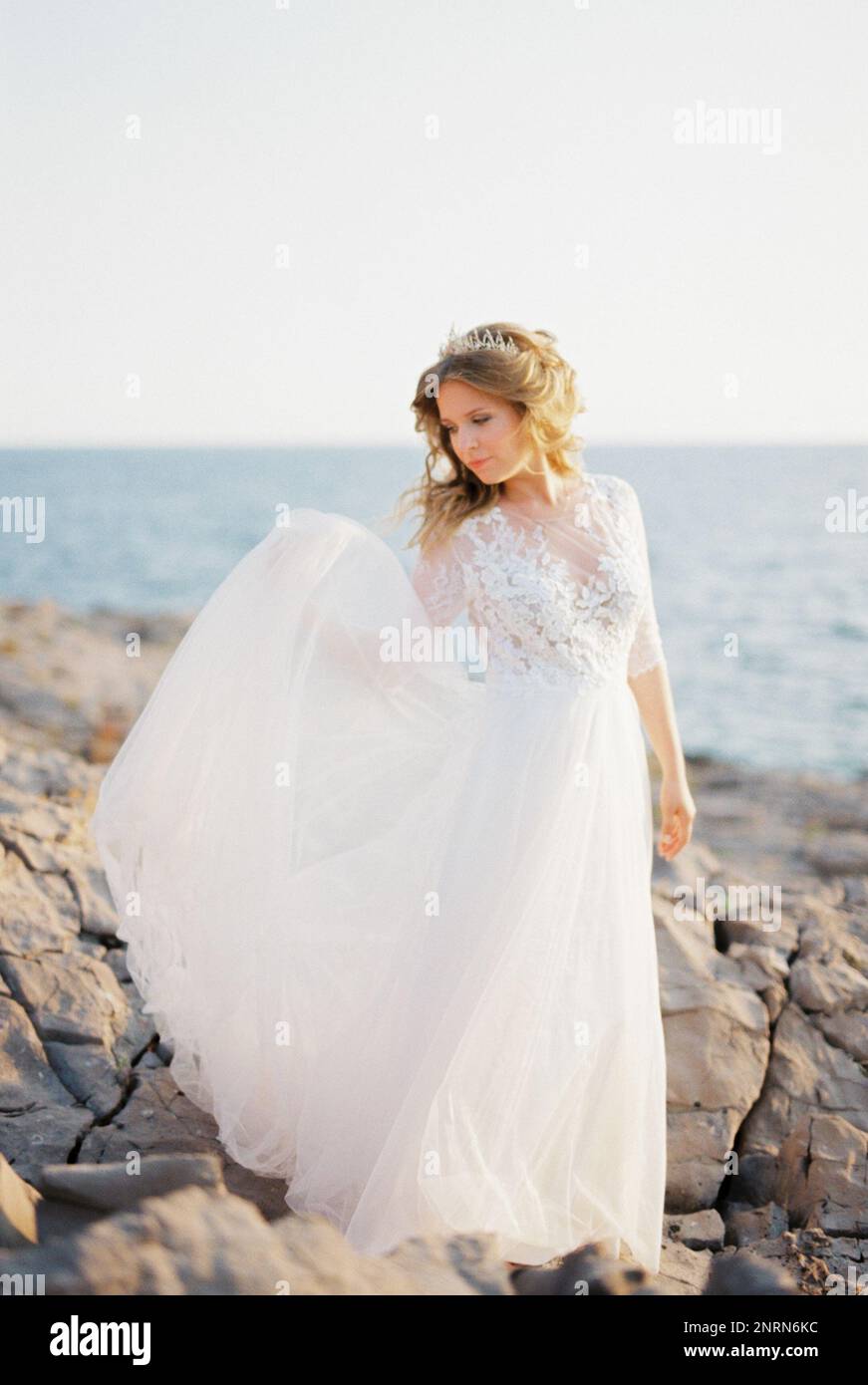 Bride raises the hem of a magnificent dress standing on the stones by ...