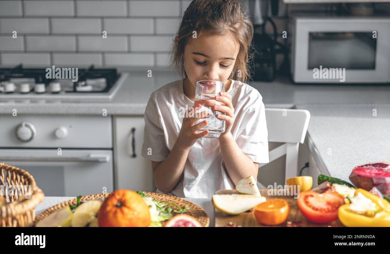 Little girl with a glass of water in a kitchen, with fruits and ...