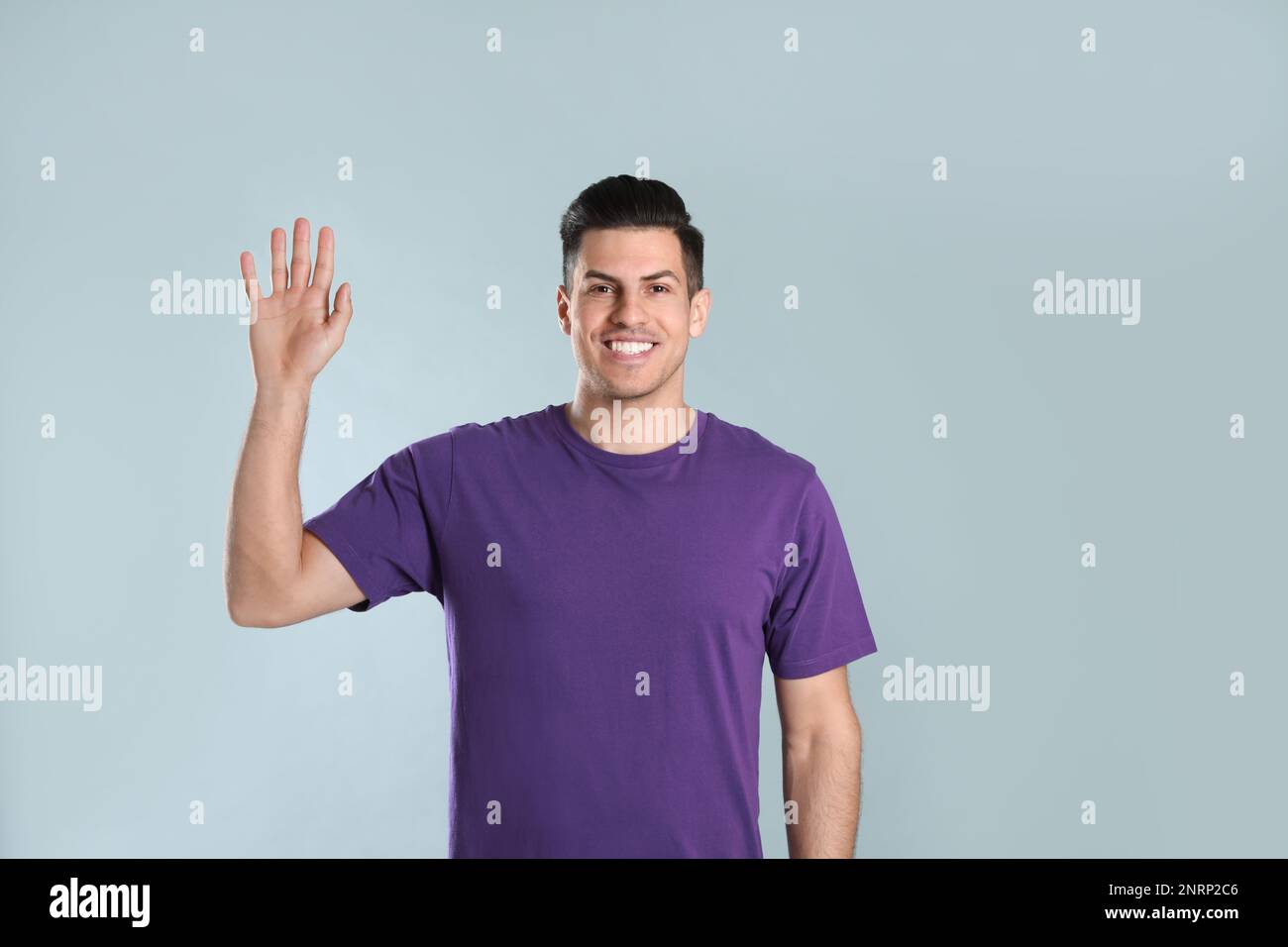 Cheerful man waving to say hello on grey background Stock Photo - Alamy