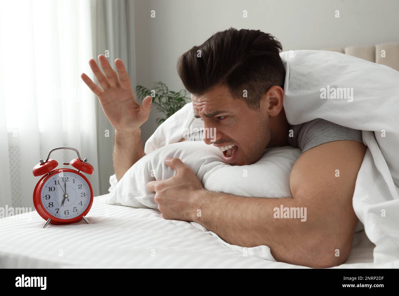 Emotional man with alarm clock in bed. Being late because of ...