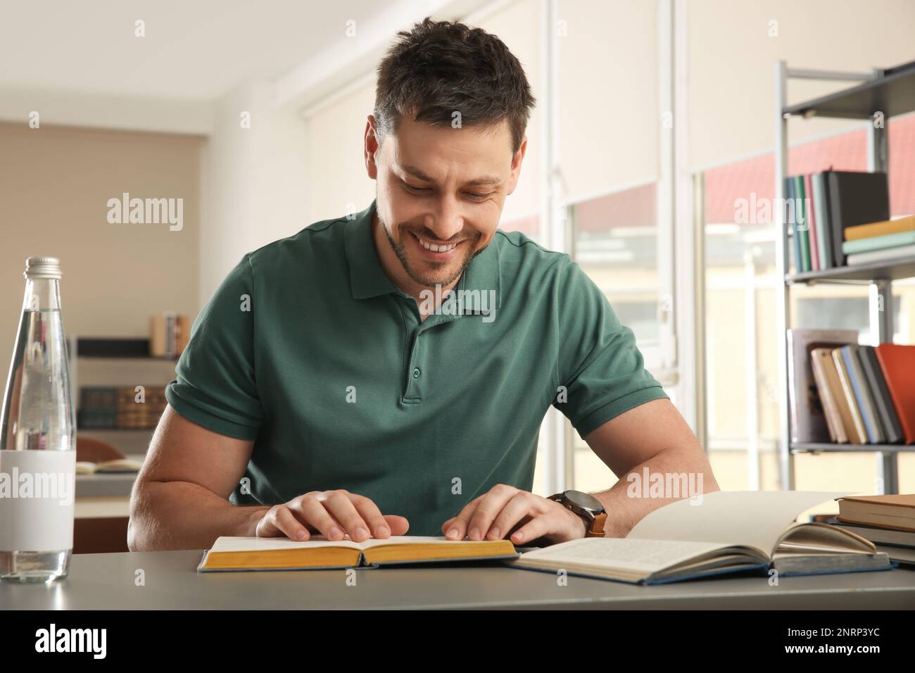 Man reading book at table in library Stock Photo - Alamy