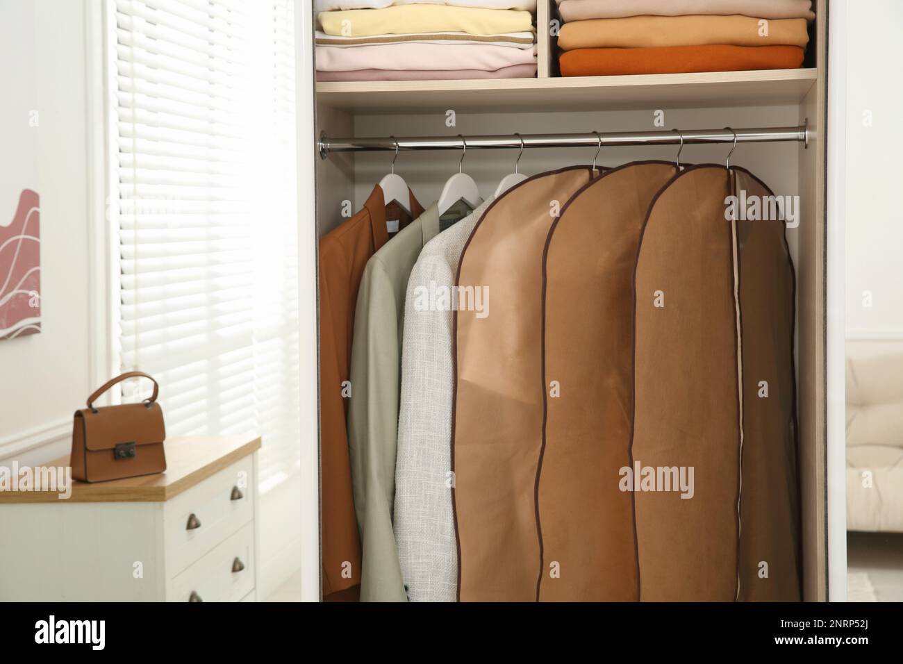 Garment bags with clothes on rack in wardrobe indoors Stock Photo - Alamy