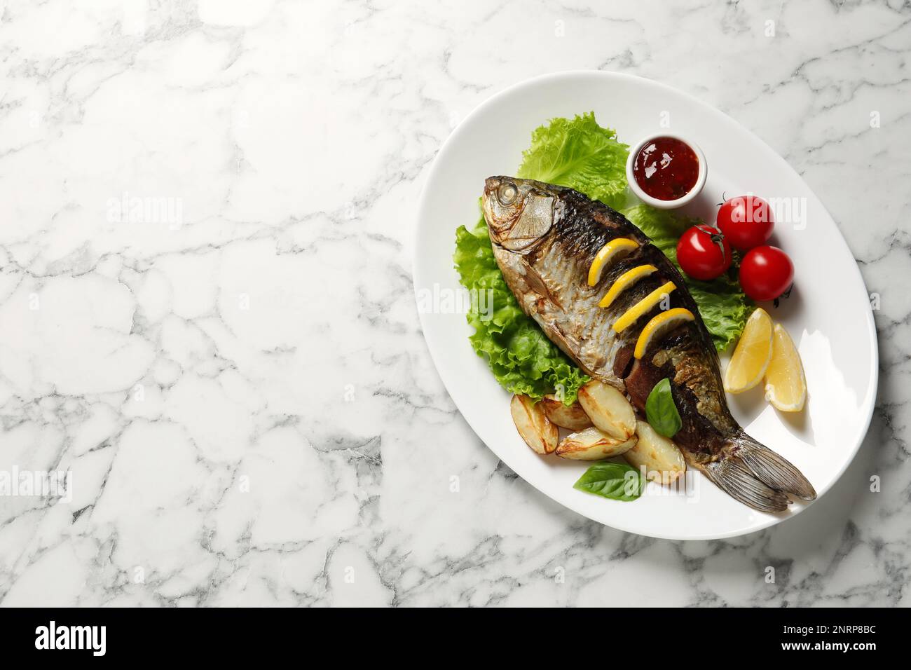 Tasty homemade roasted crucian carp with garnish on white marble table ...