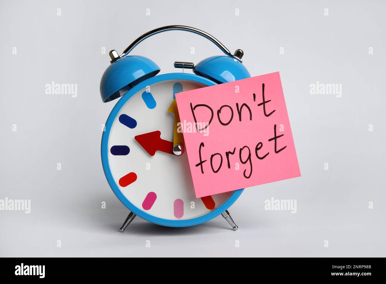 Alarm clock and reminder note with text Don't forget on light grey ...