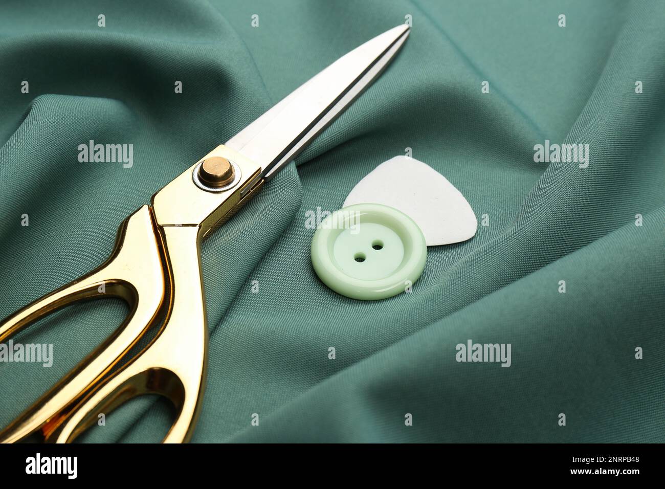Scissors, button and tailor's chalk on green fabric, closeup Stock ...
