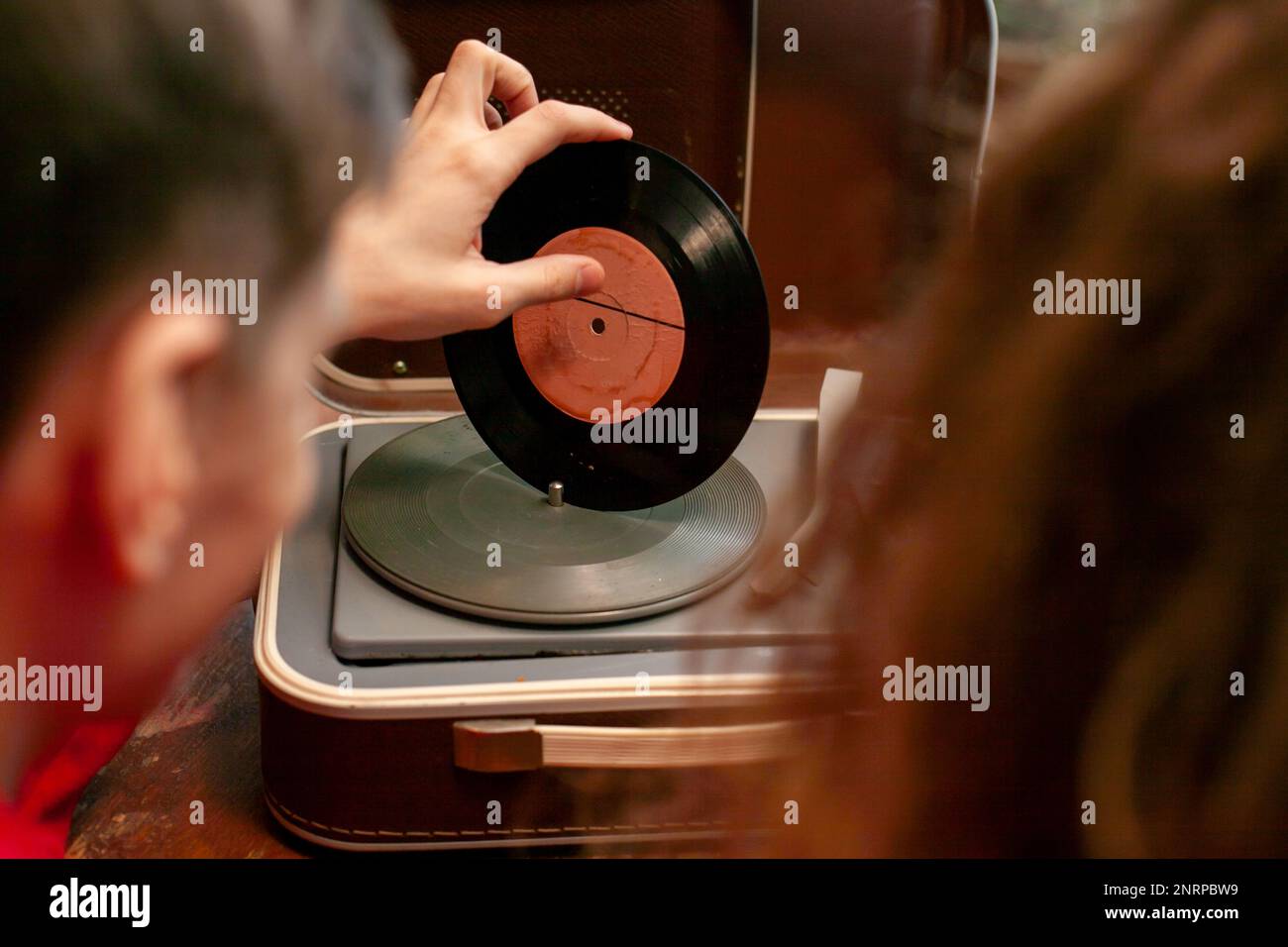 A young man holds a vinyl record in his hand on a turntable, rear view ...