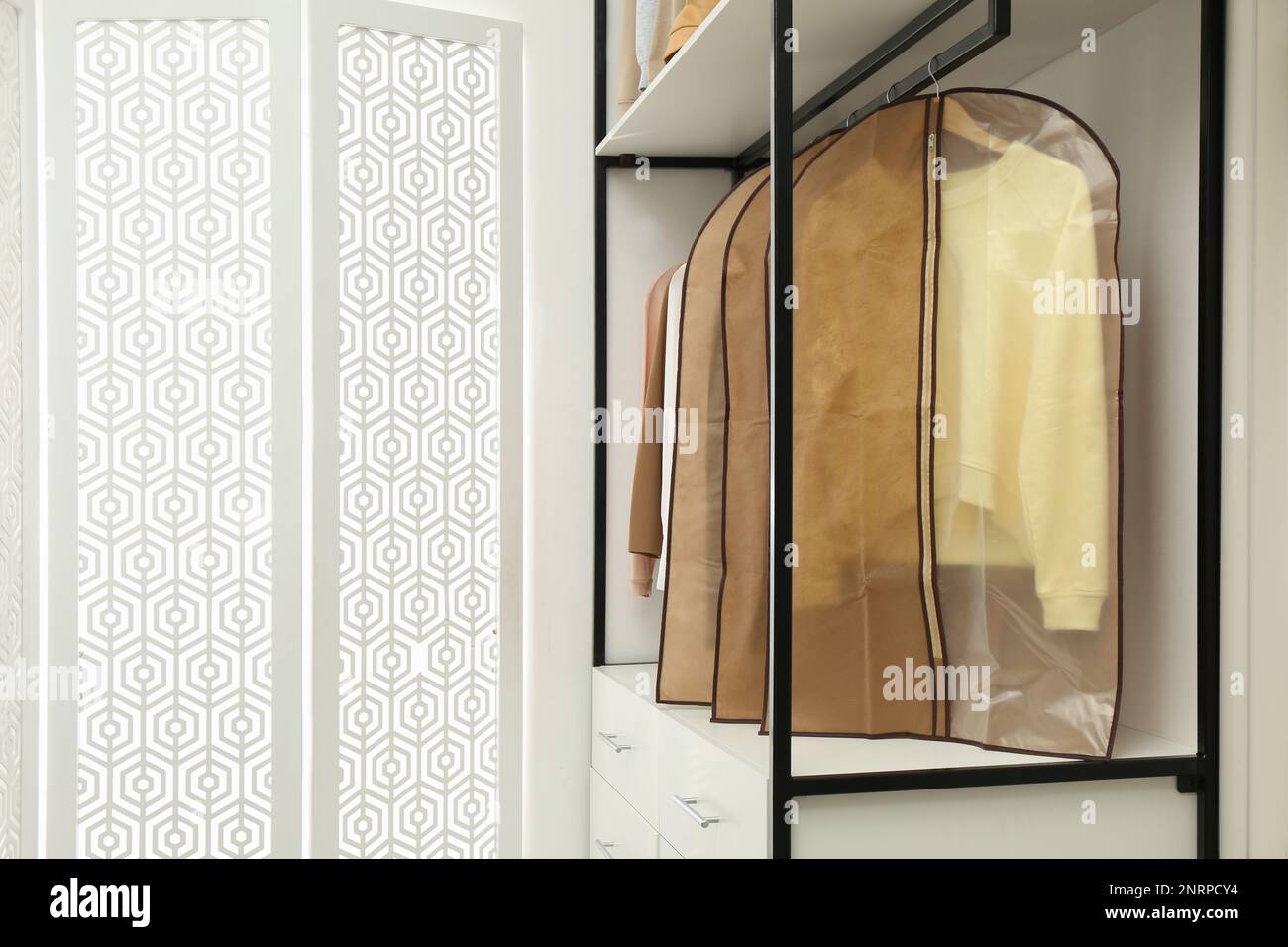 Garment bags with clothes on rack in dressing room. Space for text ...